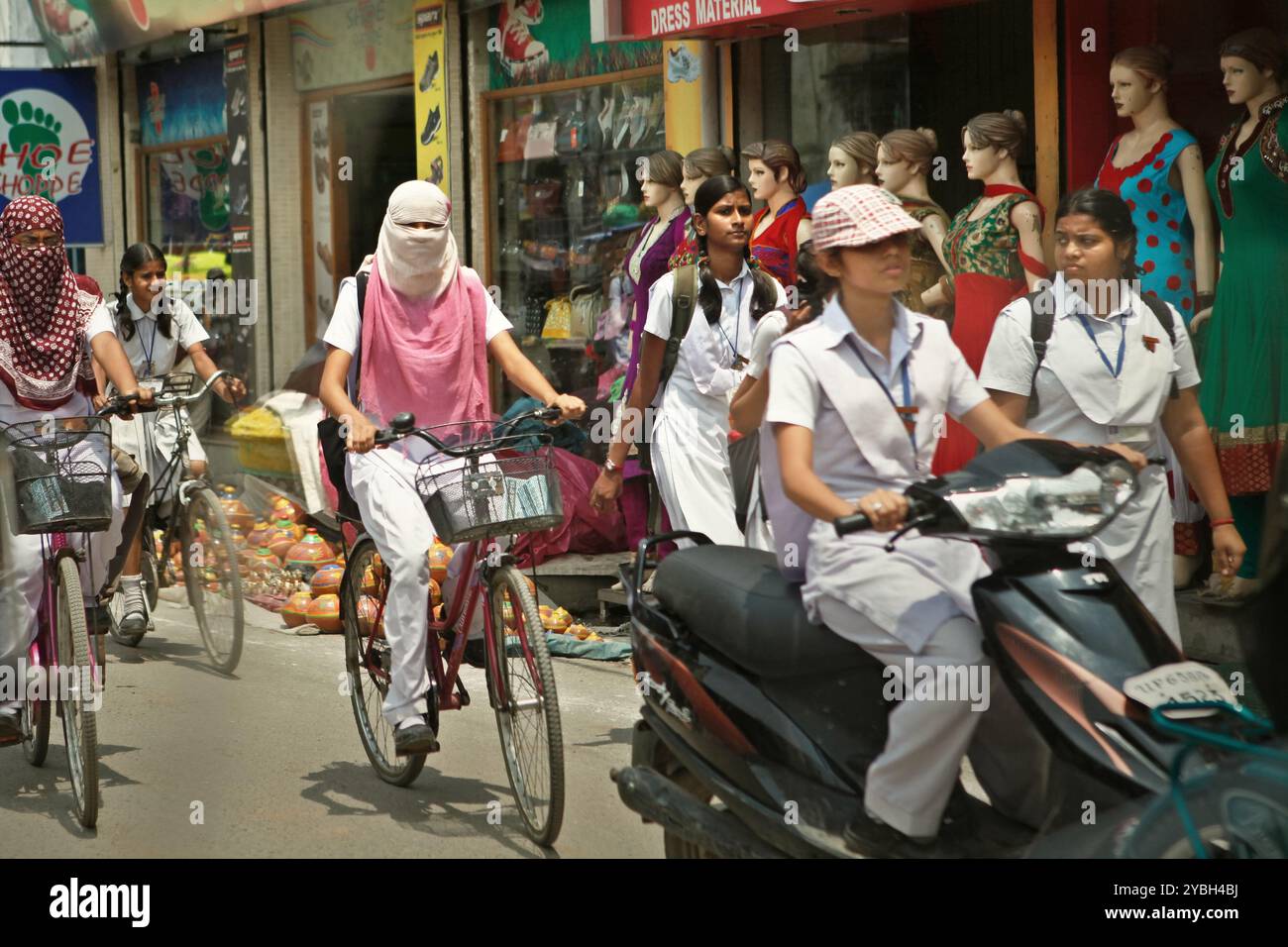 Female students cycling down a road through heavy traffic in Varanasi ...