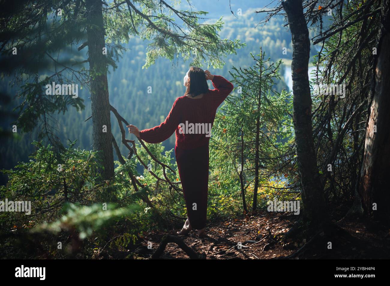 Standing among tall trees, a woman gazes at the breathtaking mountain ...
