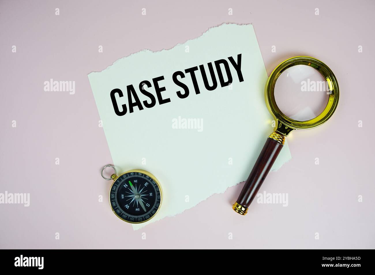 Case Studies text written on paper torn with compass and magnifying glass top view on pink ...