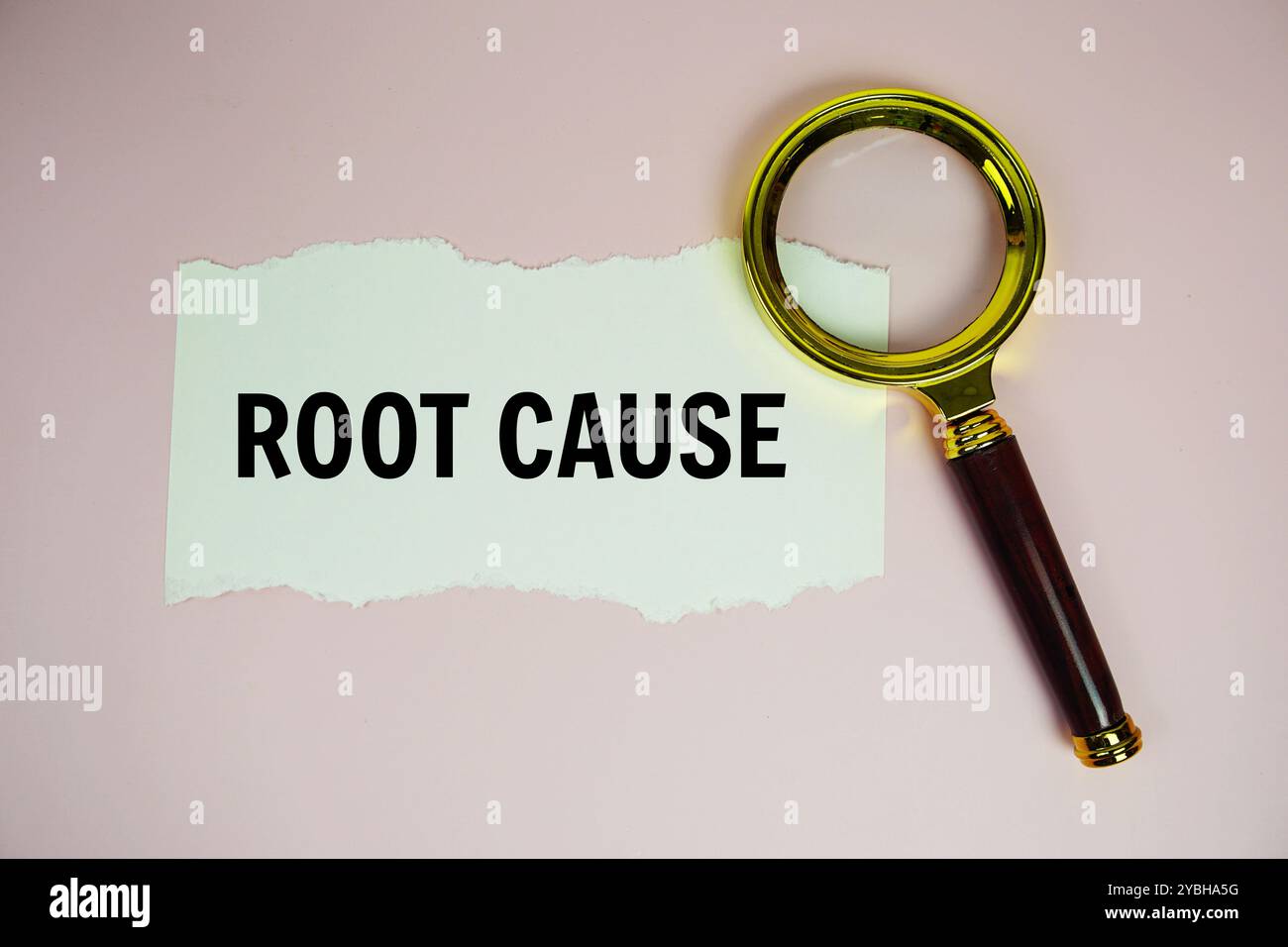 Root Cause text on paper torn with magnifying glass top view on pink ...