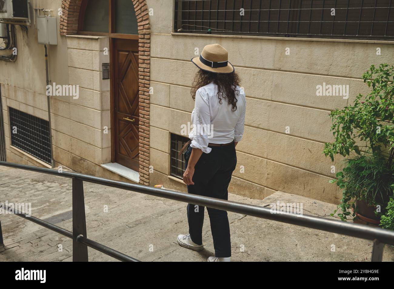 A person in a white shirt and straw hat walks down a quaint alley with ...