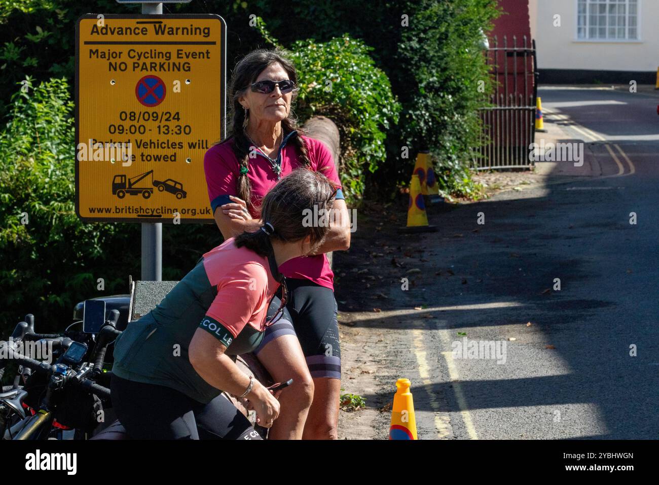 Two mature women cyclists wait by a yellow advance warning sign for the ...