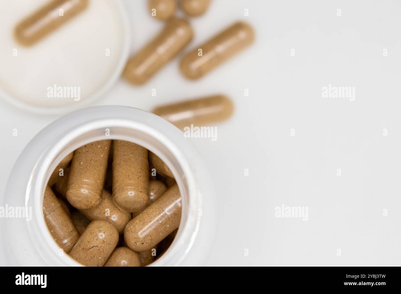 Herbal medicine capsules spilling from an open bottle onto a white ...