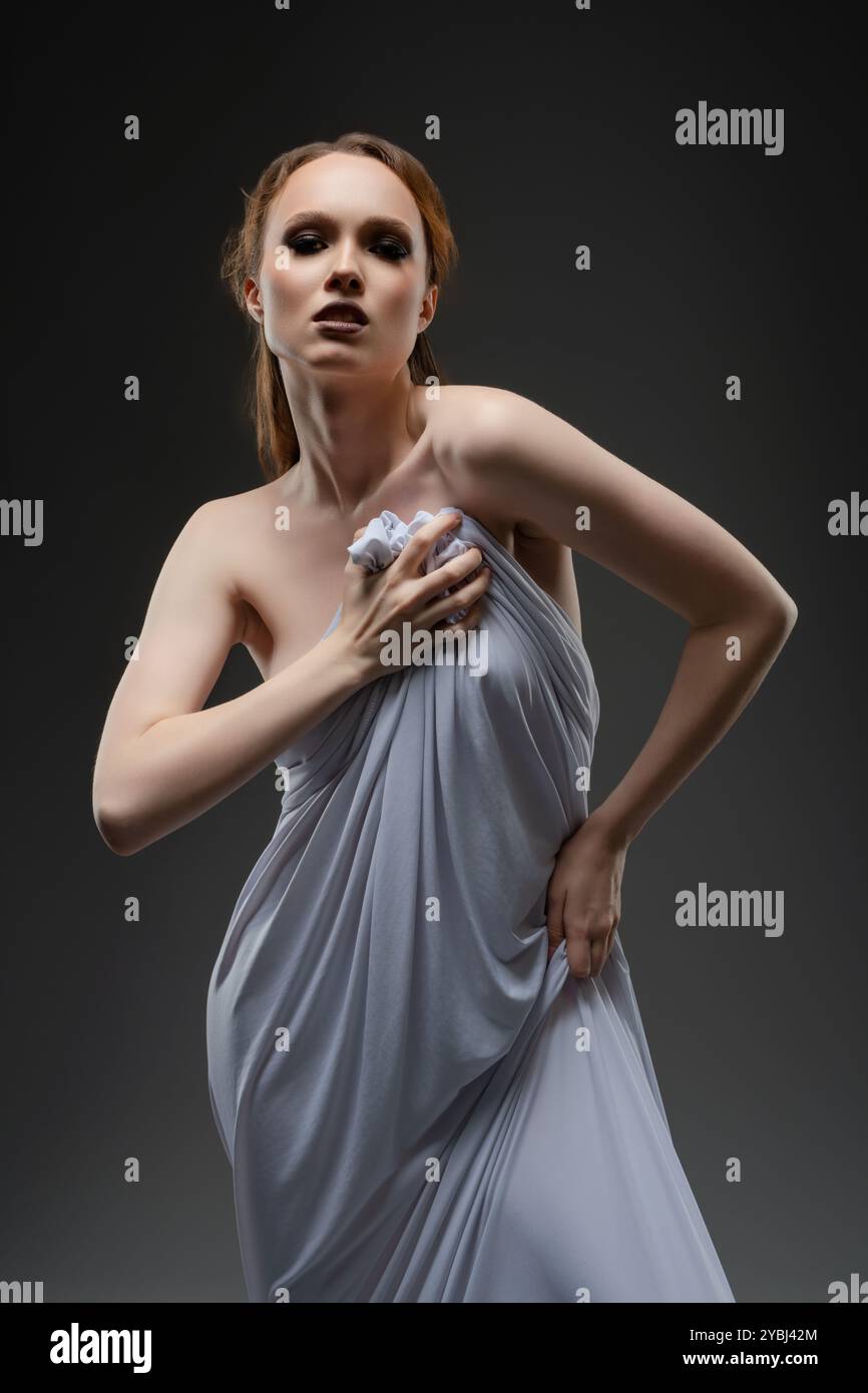 Elegant model draped in light fabric poses dramatically in studio ...