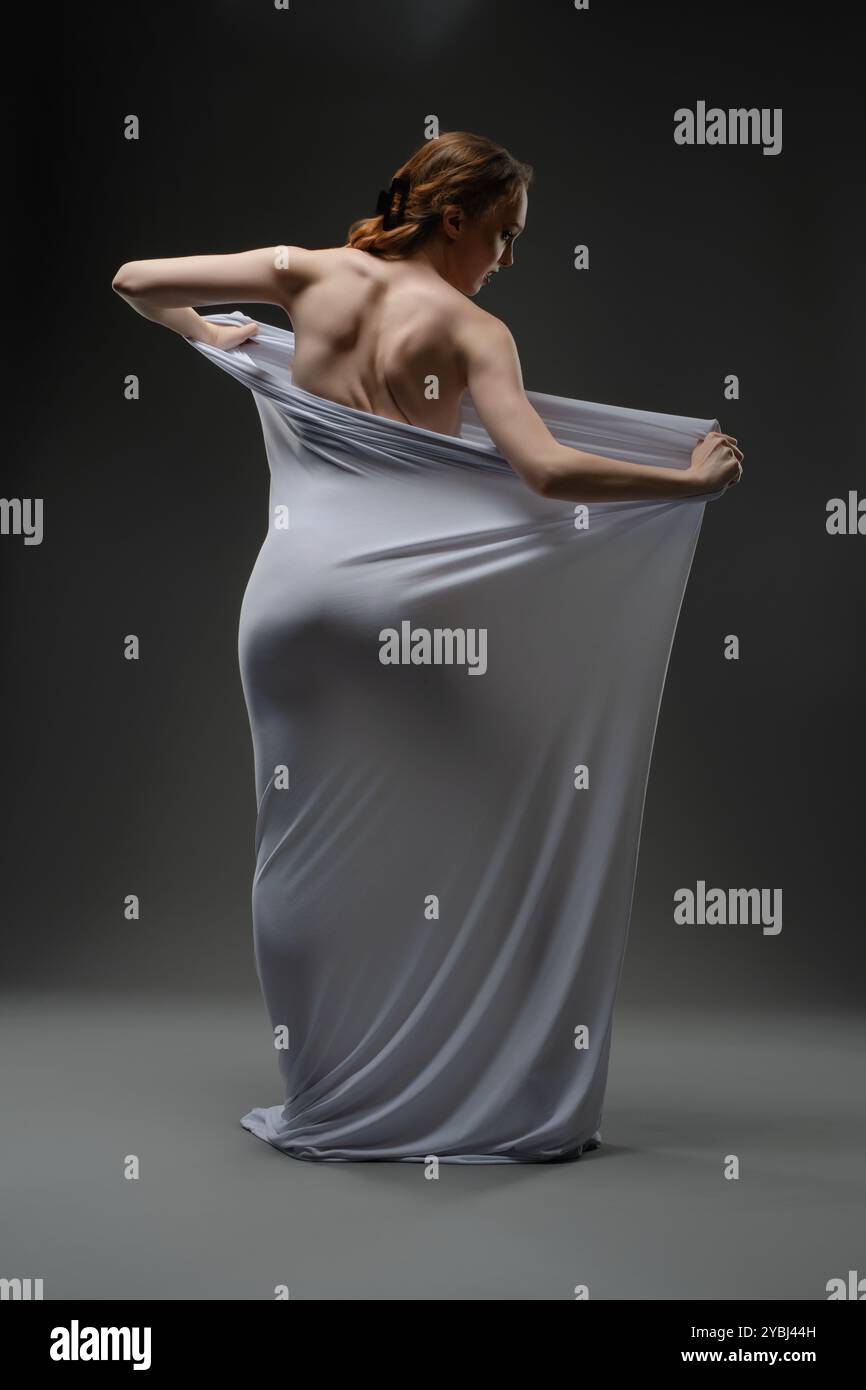 A woman elegantly draping a fabric over her body in a studio setting ...
