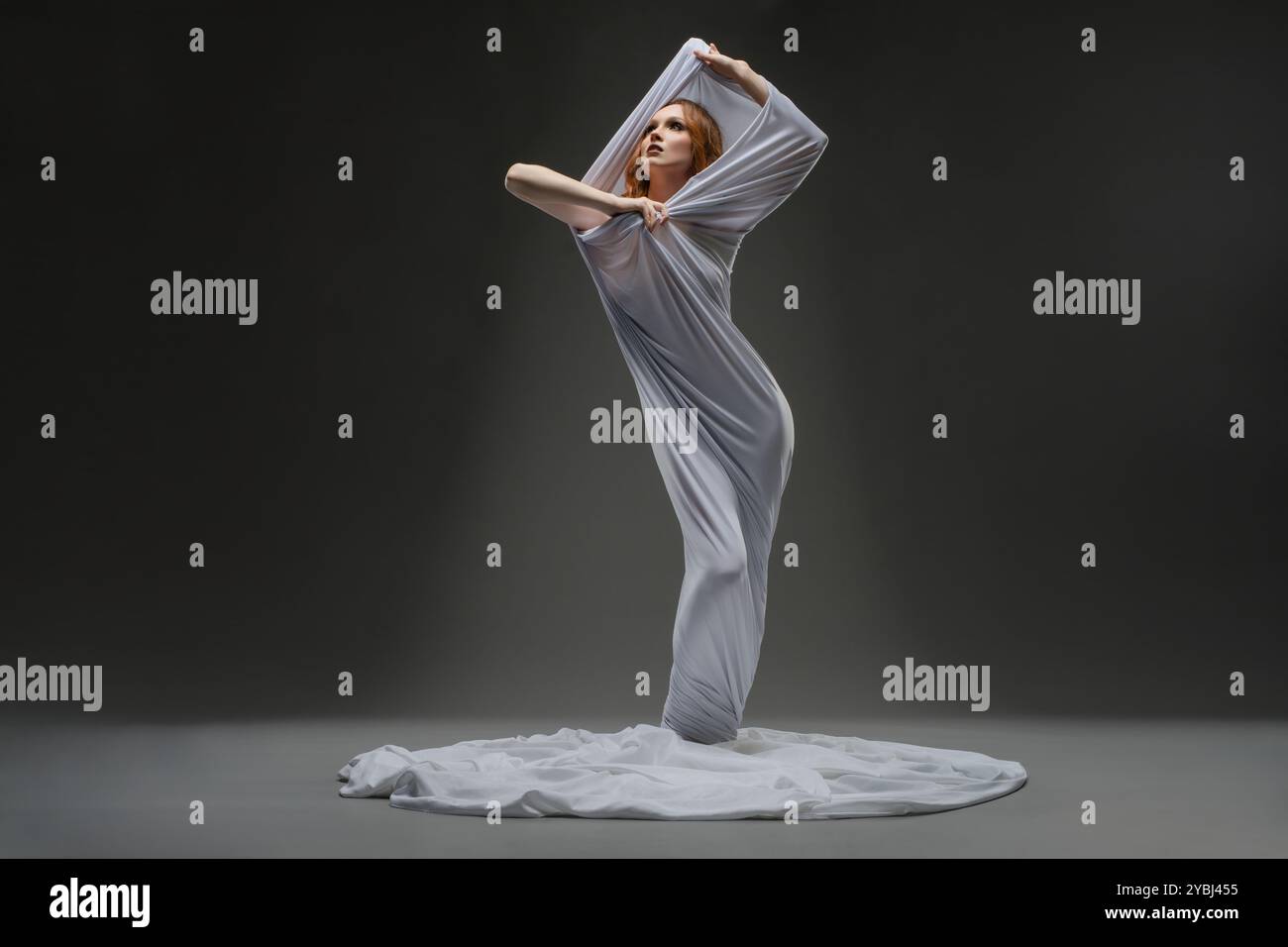 Model poses elegantly in a flowing gray garment against a dark backdrop ...