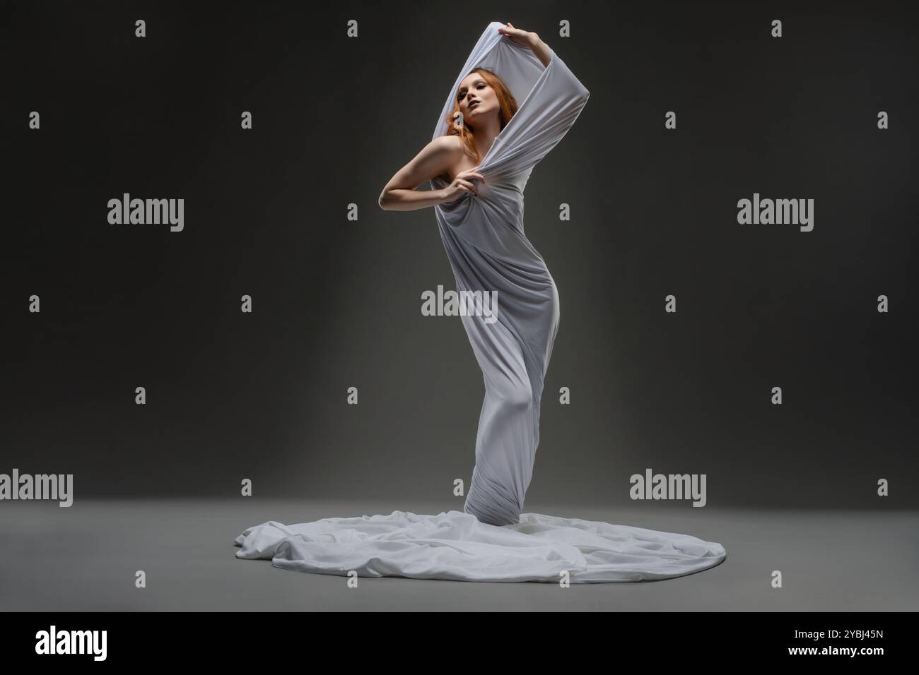 Elegant model in a flowing white dress poses dramatically in studio ...