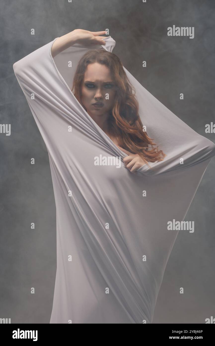 Female model draped in sheer fabric poses dramatically in a misty ...