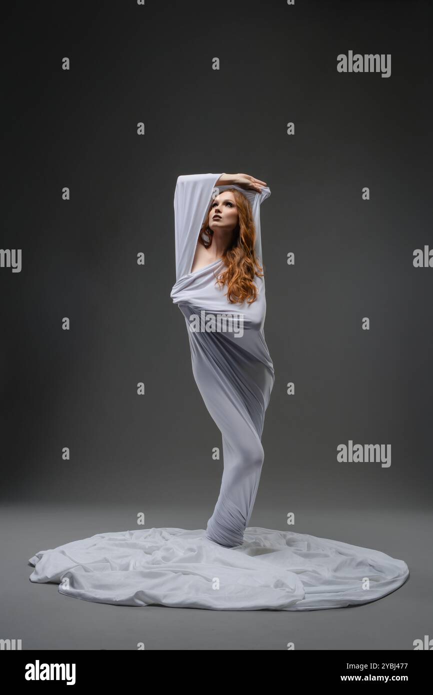A dancer in a flowing white fabric striking an elegant pose in a studio ...