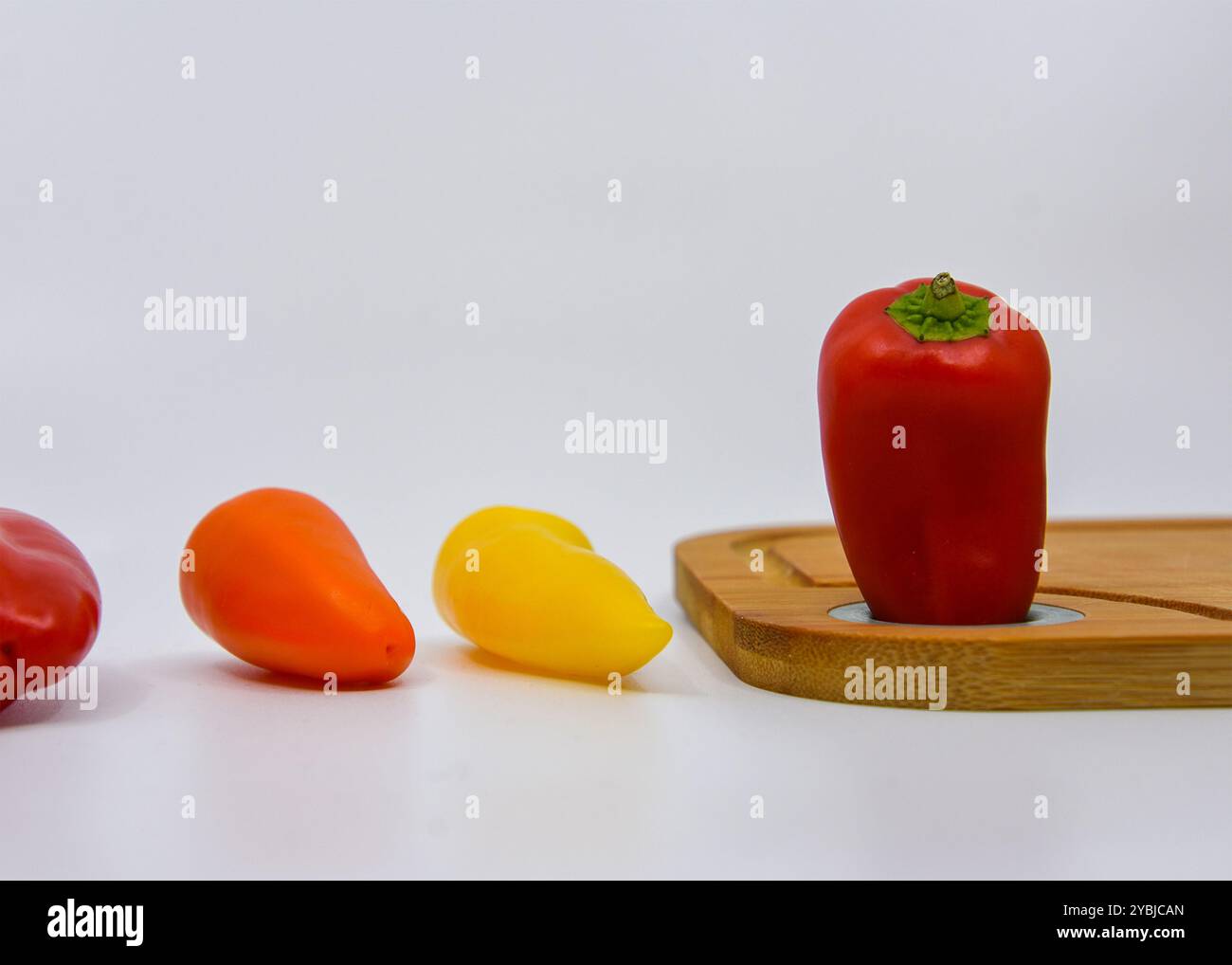 A bright red pepper is resting on the surface of a wooden cutting board ...
