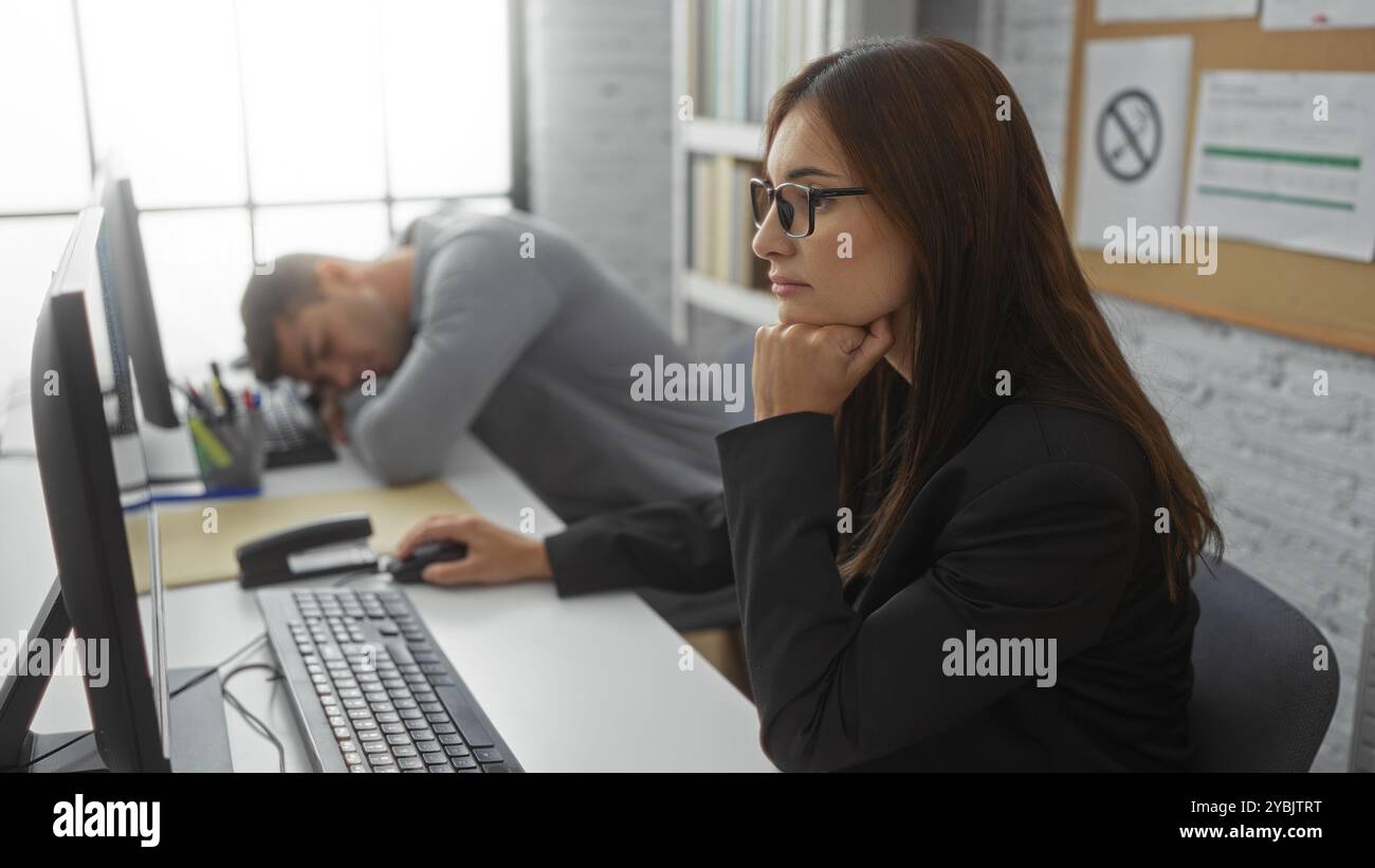 Woman working on desktop computer in office while man sleeps beside in ...