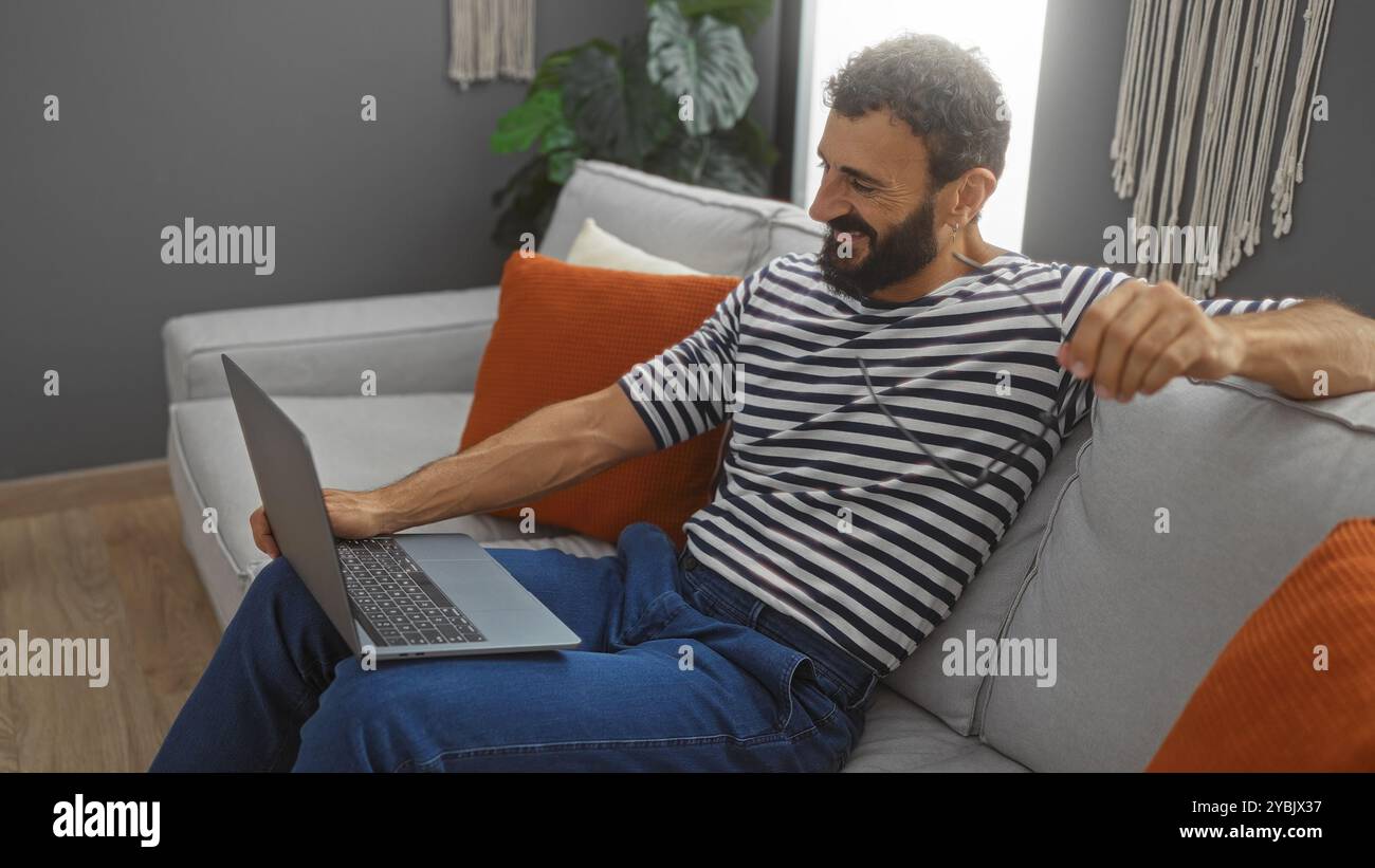 Handsome, young, hispanic man with a beard relaxing on a couch in a cozy apartment living room ...