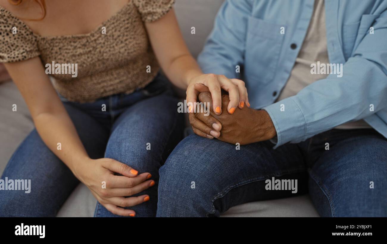 Interracial couple sitting together at home holding hands in a living ...