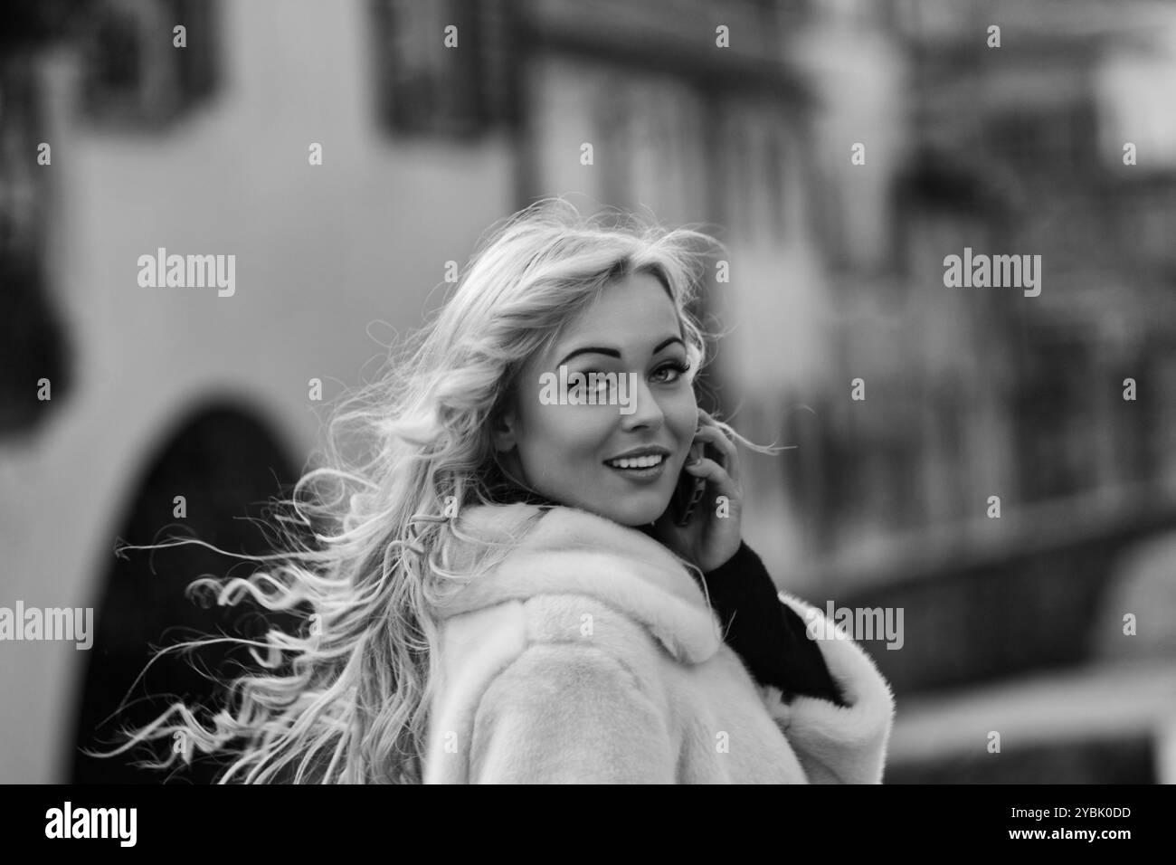Smiling young woman with long, wind blown hair, wearing a fur coat, is ...