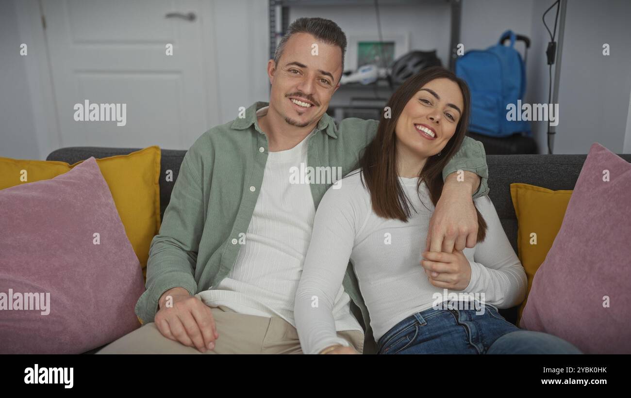 A smiling couple sits closely on a sofa in their modern living room ...