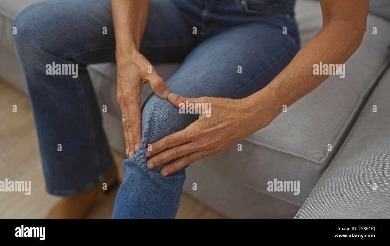 A middle-aged woman sitting indoors experiences knee pain, grasping her ...