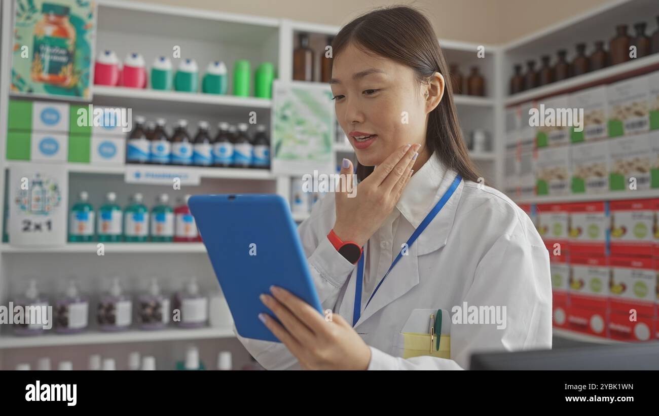 A young asian woman pharmacist in white lab coat using a tablet inside ...