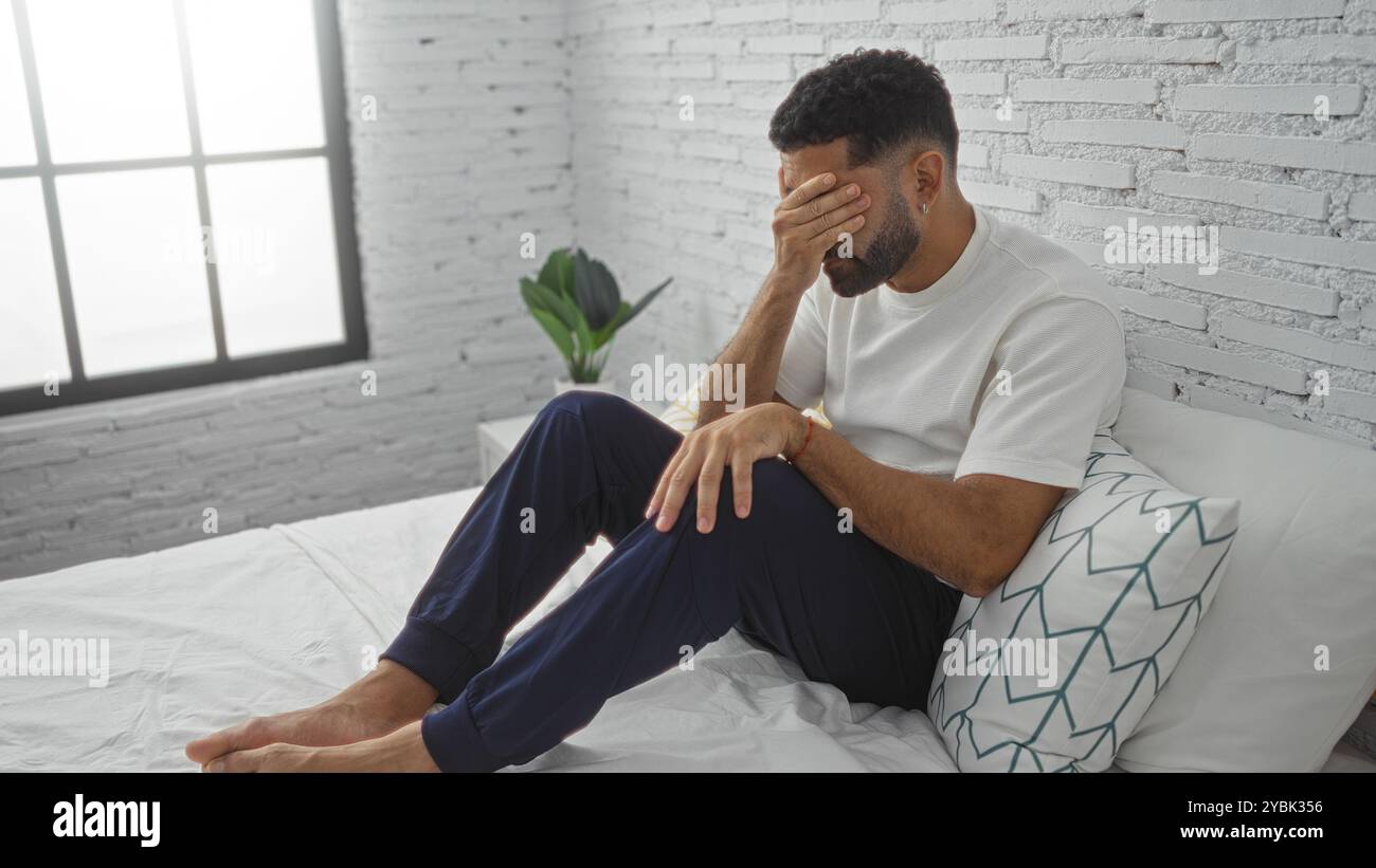 Young man sits on bed in modern bedroom with white brick wall covering ...