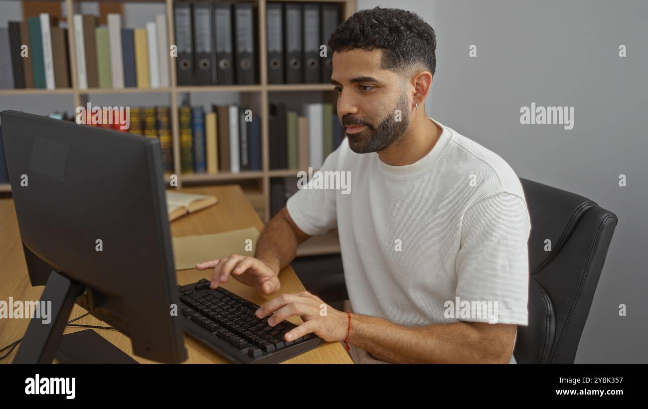 Young man typing in an office setting surrounded by books and folders ...
