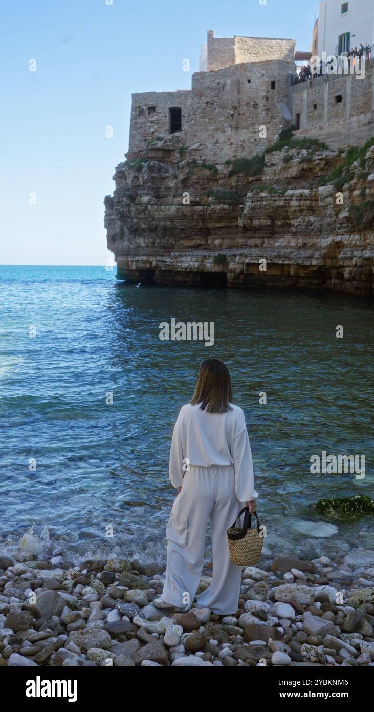 Young hispanic woman standing on a rocky beach in polignano a mare ...