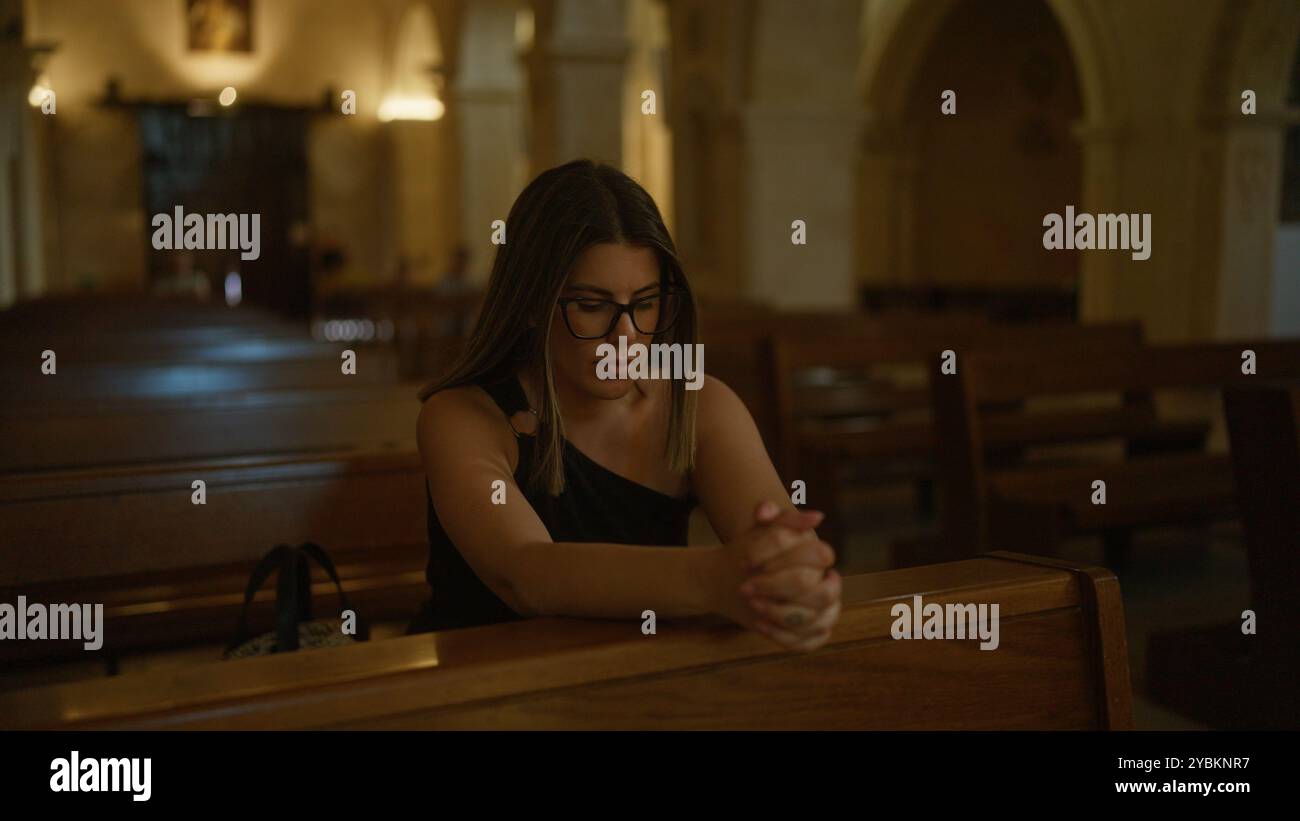 A young hispanic woman prays in a christian church in italy, surrounded ...