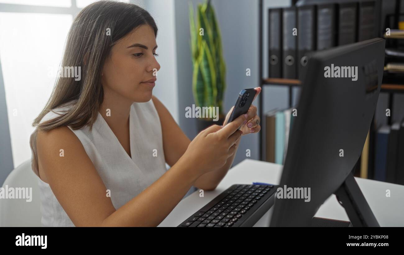 Woman in office using smartphone with computer on desk and files in ...