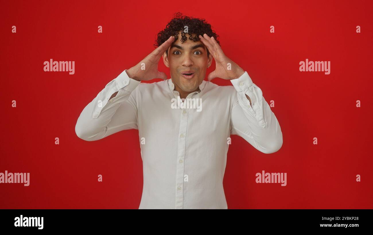 Surprised young hispanic man in white shirt against solid red ...