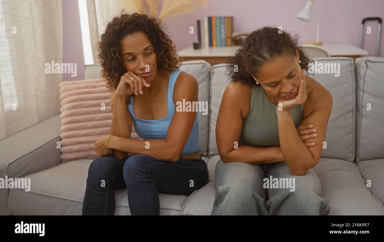 Two women sitting thoughtfully together on a couch in a cozy living room, highlighting their ...