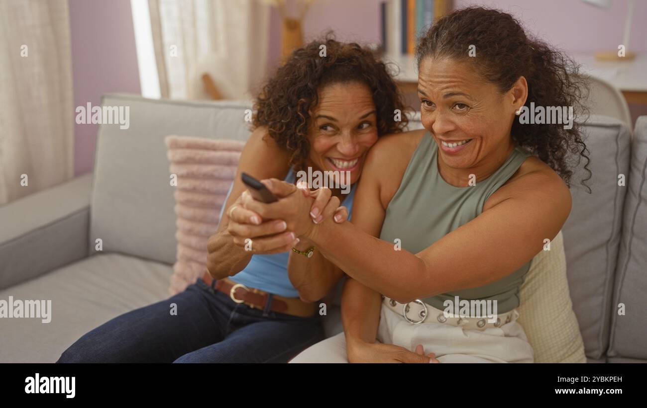 Two hispanic women laughing and playfully fighting over a tv remote in ...