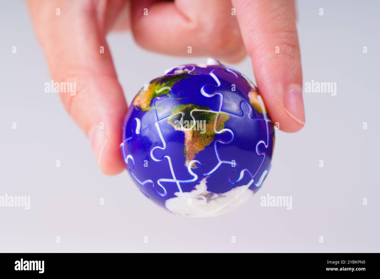 Hand grasping a globe designed as a 3D puzzle piece, representing ...