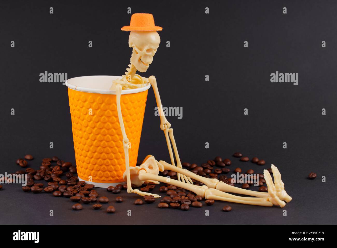 Skeleton sitting beside bright orange coffee cup with coffee beans ...