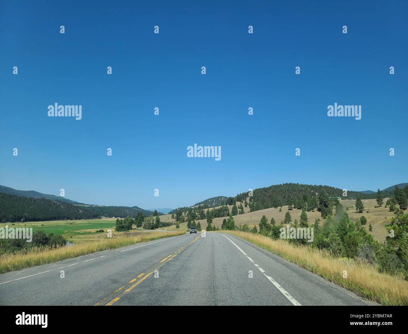A long, straight road stretches through a vast, open landscape with ...