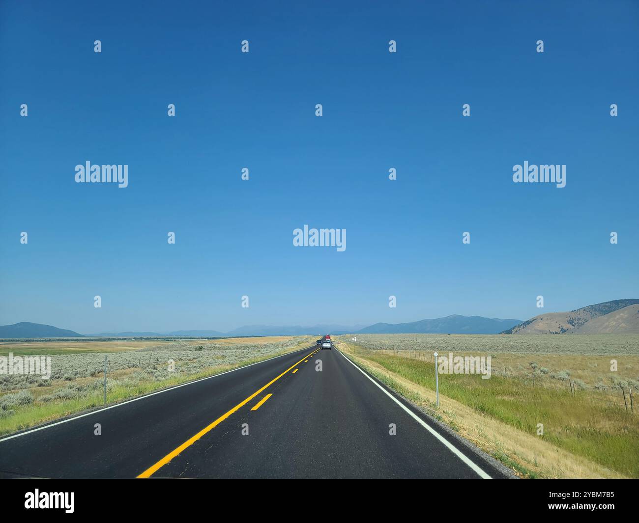 A long, straight road stretches through a vast, open landscape with ...