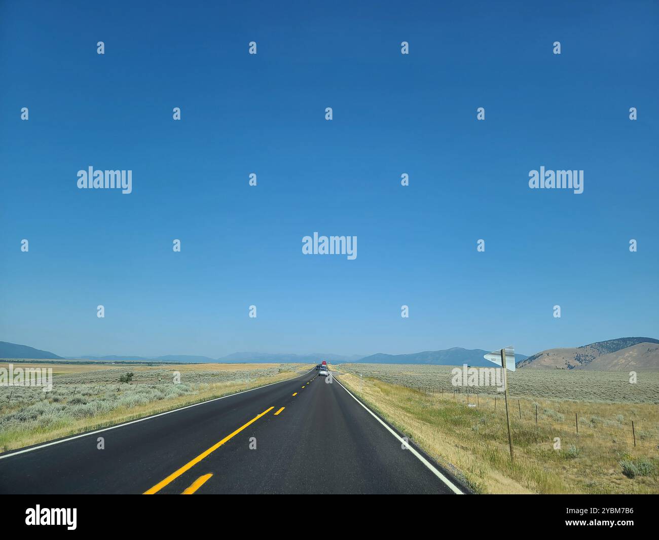 A long, straight road stretches through a vast, open landscape with ...