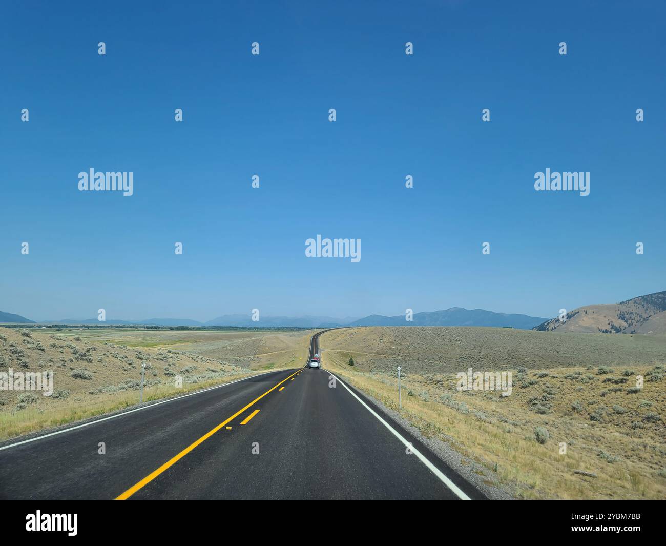 A long, straight road stretches through a vast, open landscape with ...