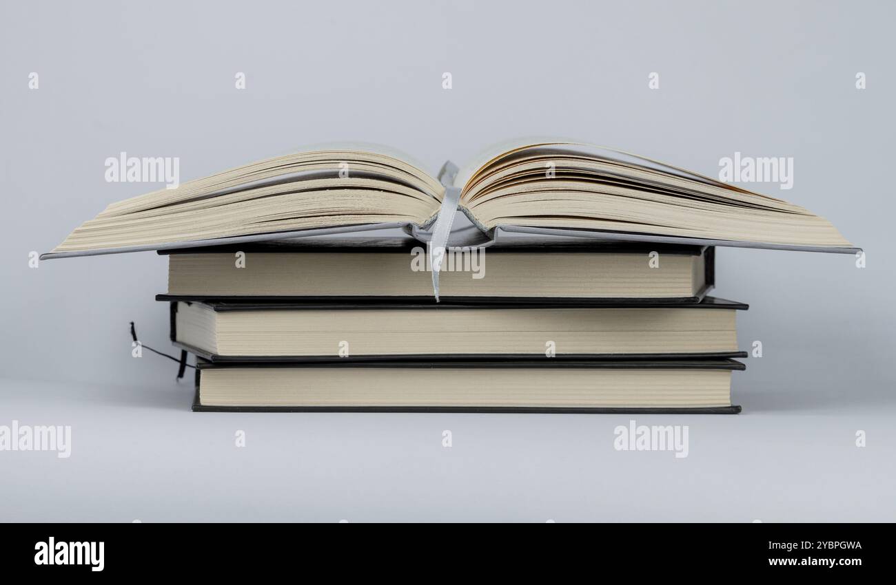 An open book rests atop a stack of three closed books Stock Photo - Alamy