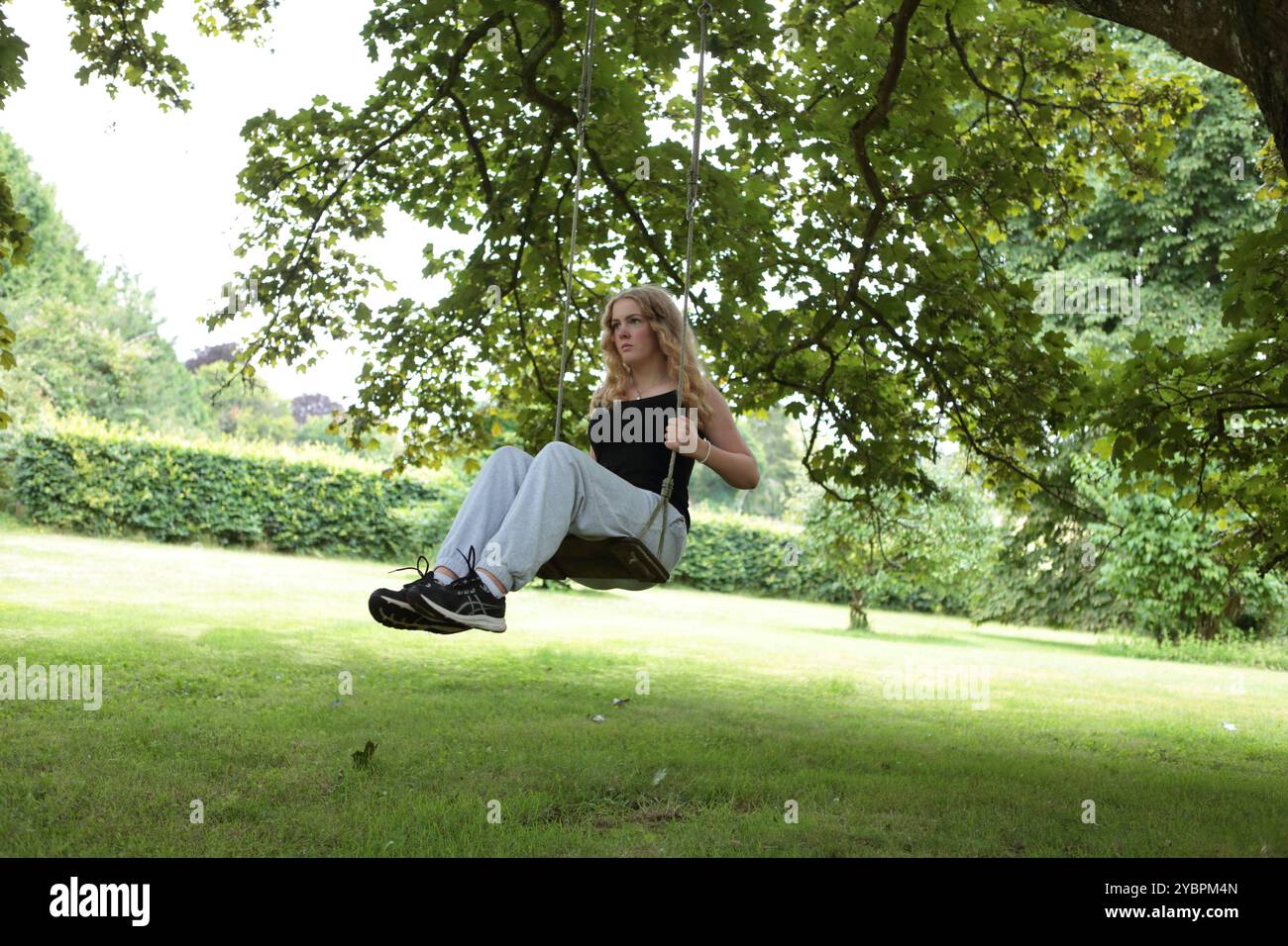 Teenage girl on swing under tree in garden in summer Stock Photo - Alamy