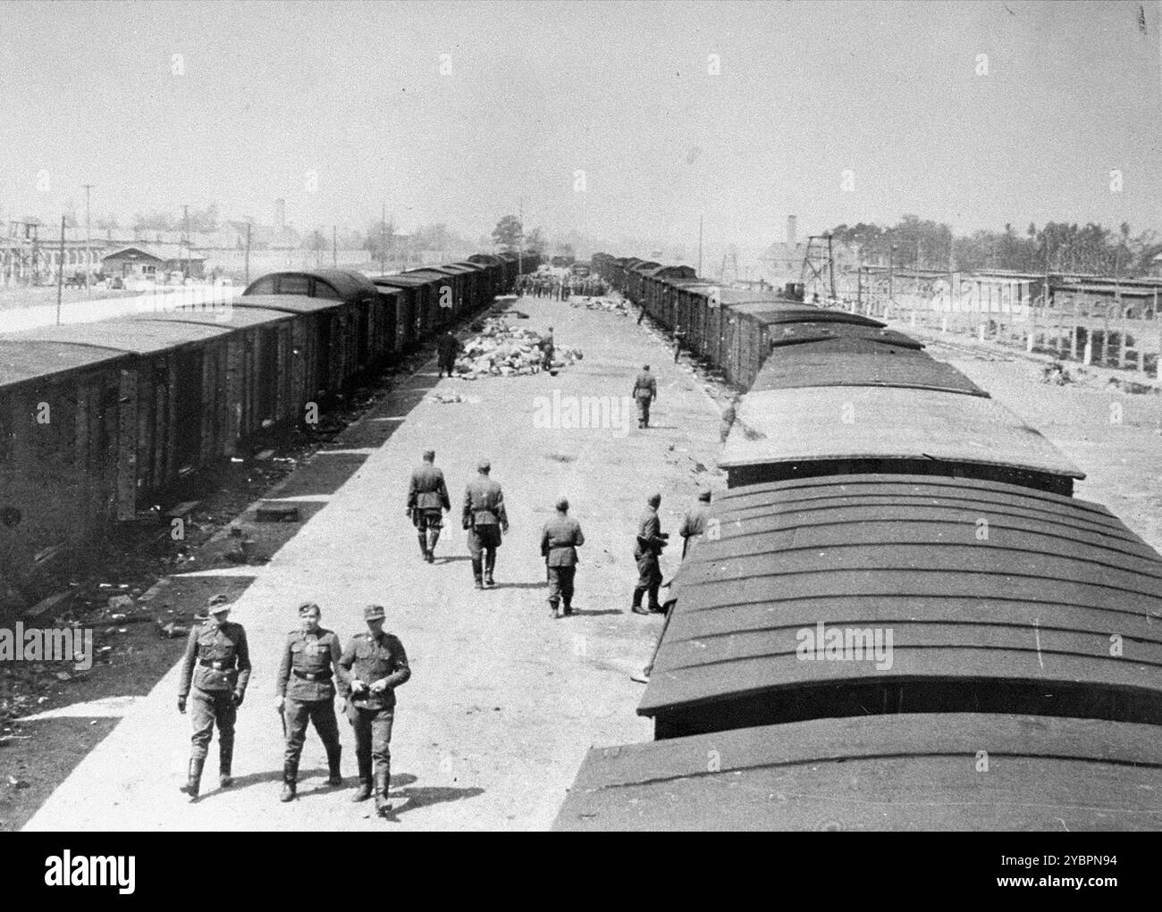 SS guards walk along the arrival ramp at Auschwitz-Birkenau. At the far ...