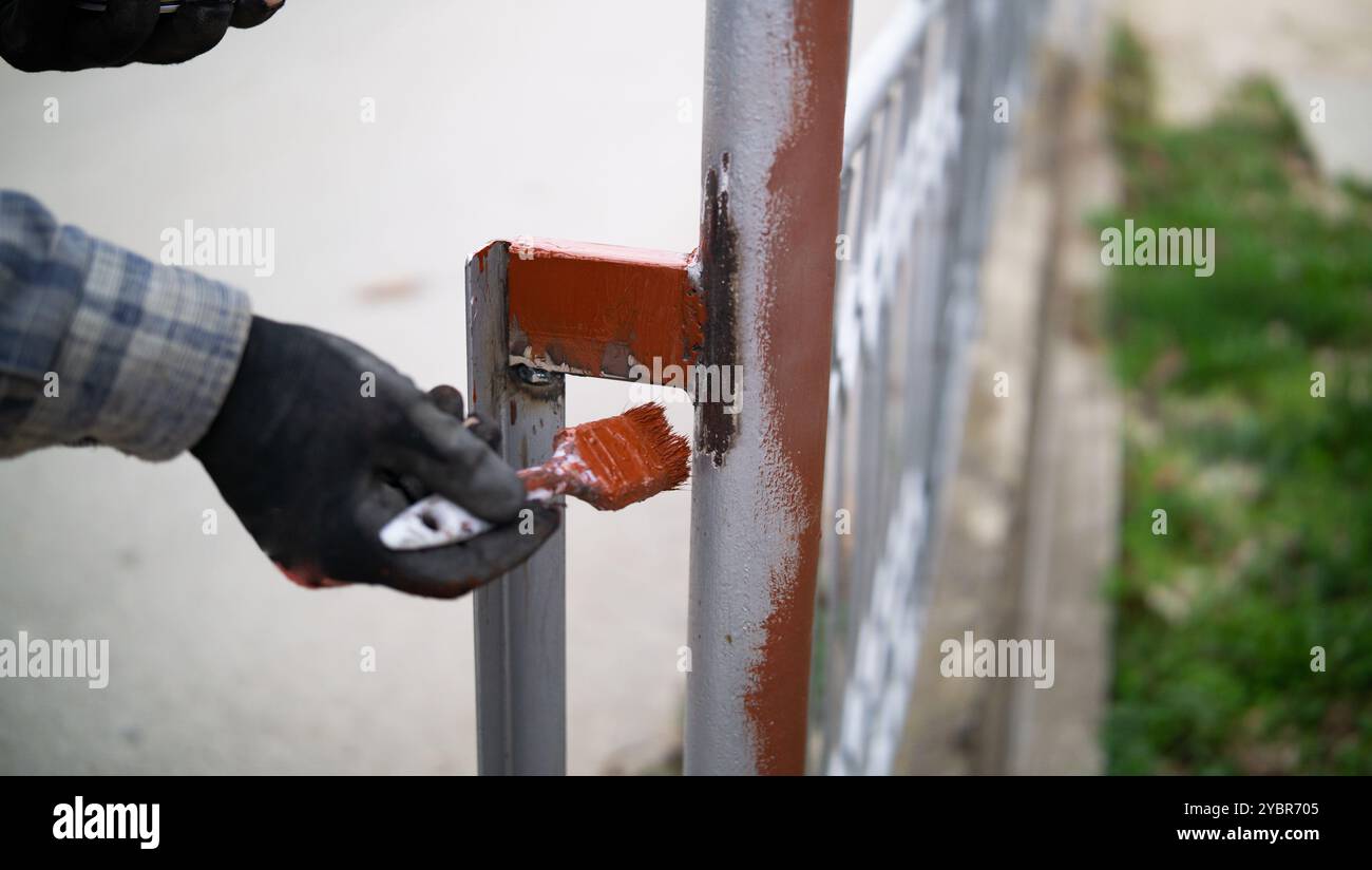 Male hand painting metal fence with a brush with red oxide metal primer ...