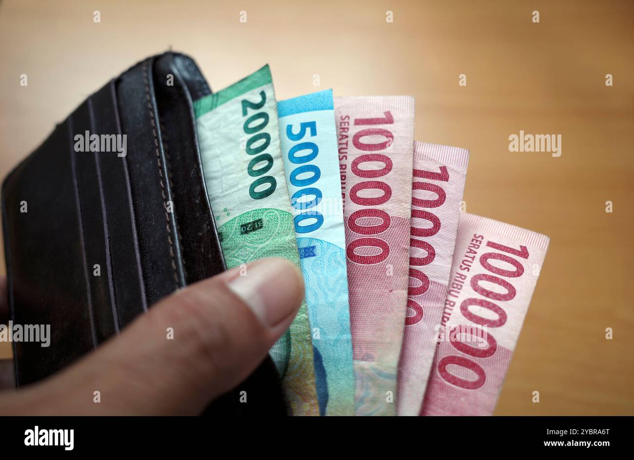 Adult finger takes Rupiah, Indonesian money from a black wallet. Saving ...