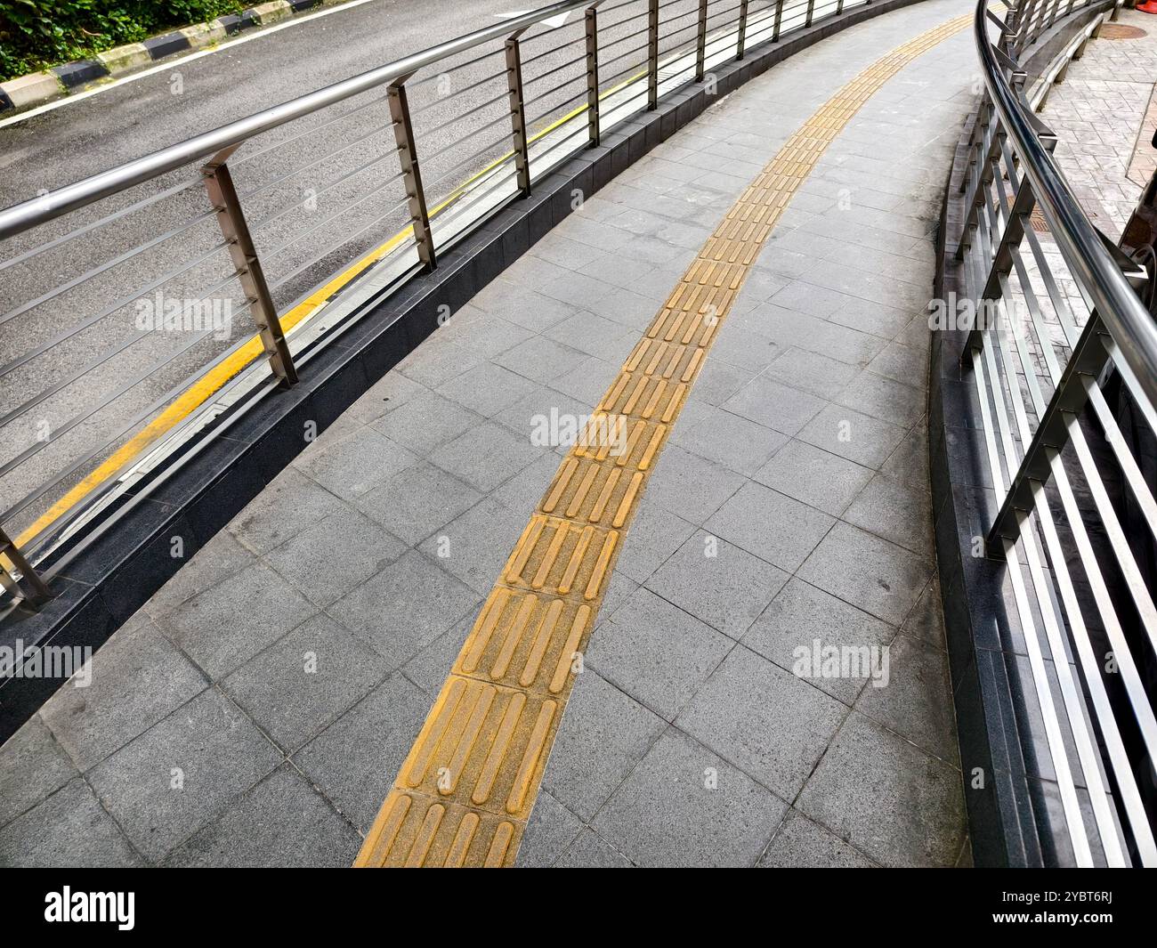 Curved path with guardrail and yellow line for blind people along the ...