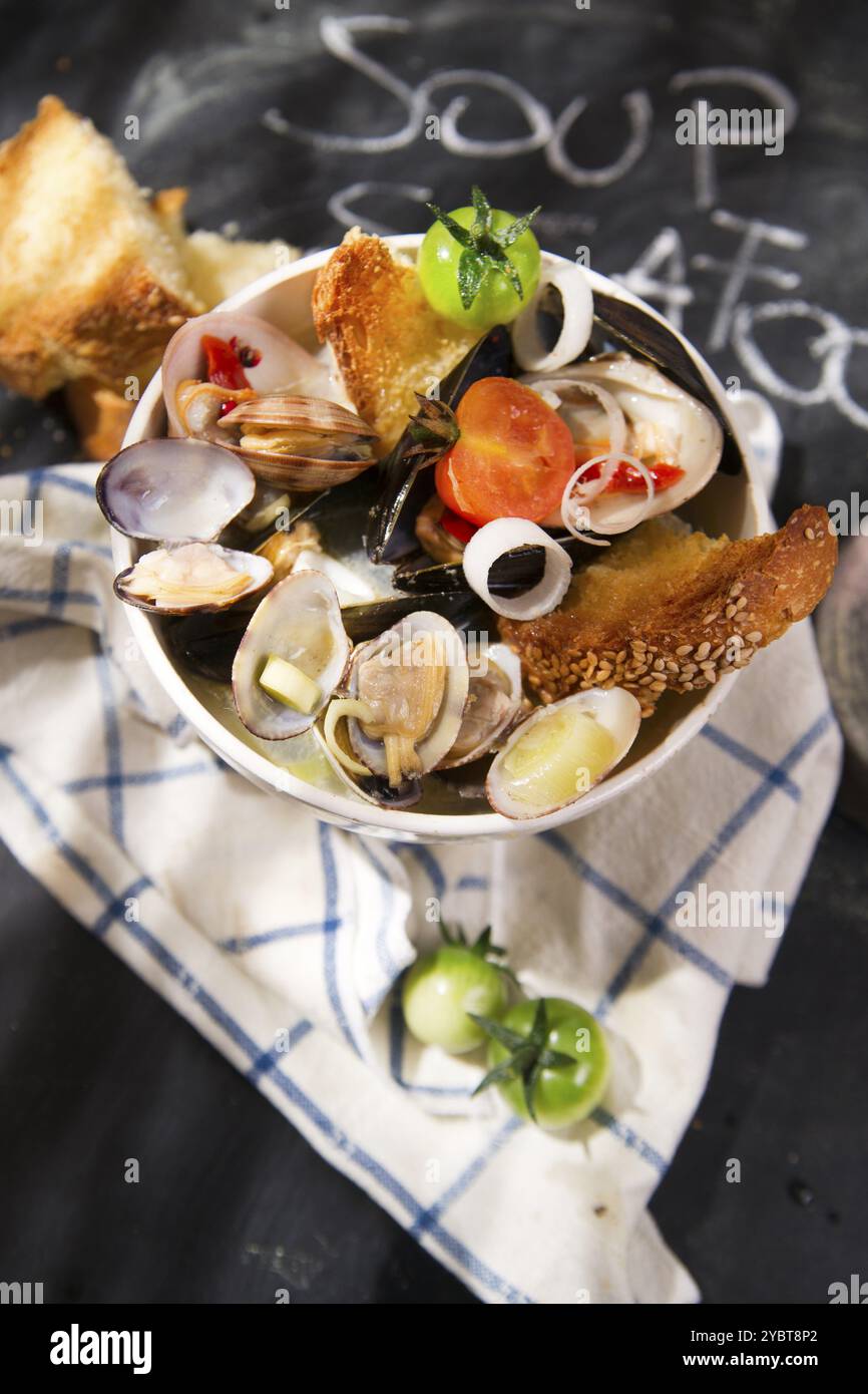 Presentation of a soup with seafood on a black background with writing ...