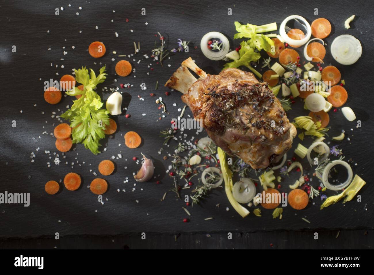 Presentation of a cooked pork shank with vegetables on stone slate ...