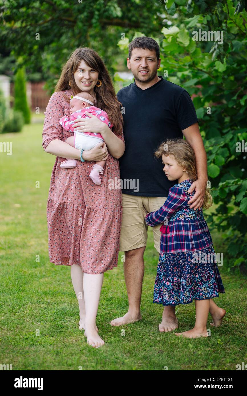 Young family happily poses barefoot in the grass with their newborn ...