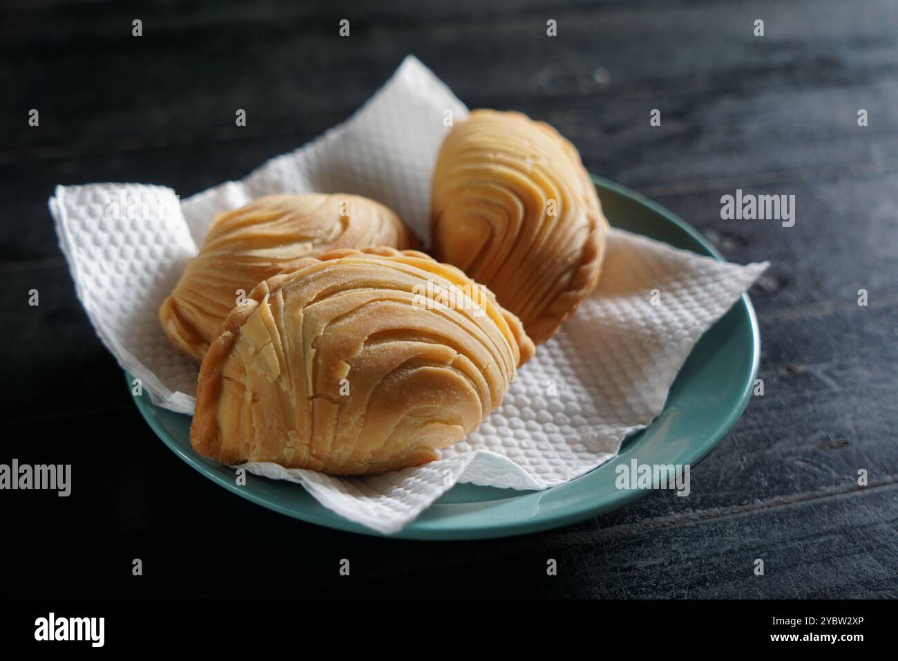 A plate of Malaysian deep fried curry puff or epok-epok isolated on dark background. Also known ...