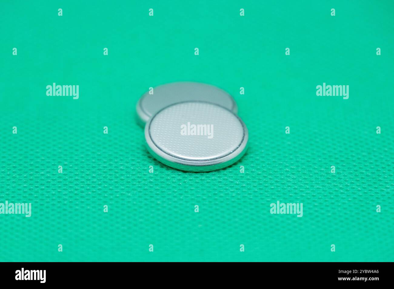 Two button cell batteries lying on a green background, representing ...