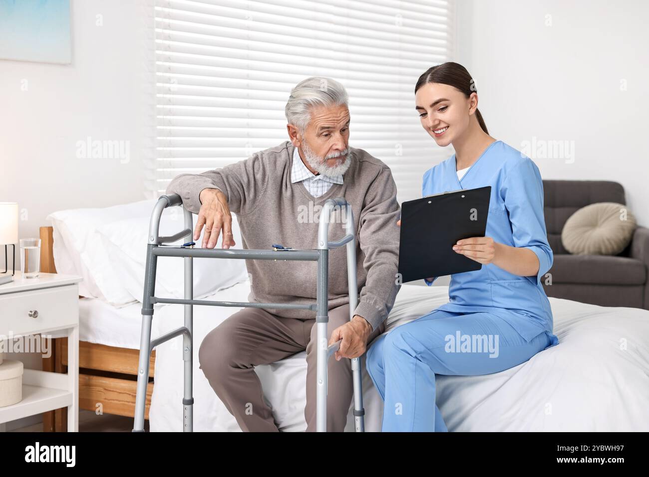 Doctor consulting senior patient with walking frame in hospital ward ...