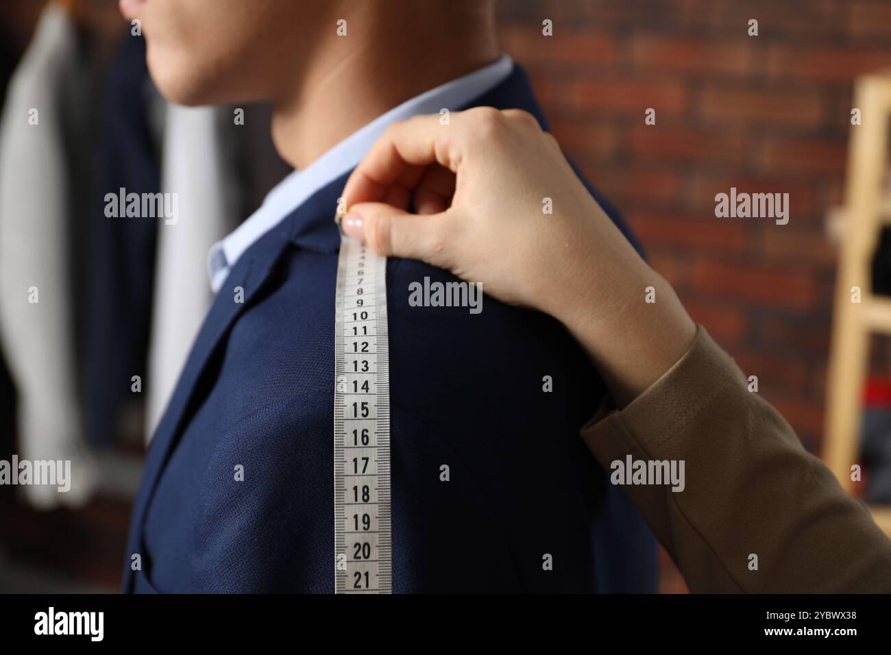 Professional tailor measuring shoulder seam length on client's jacket ...
