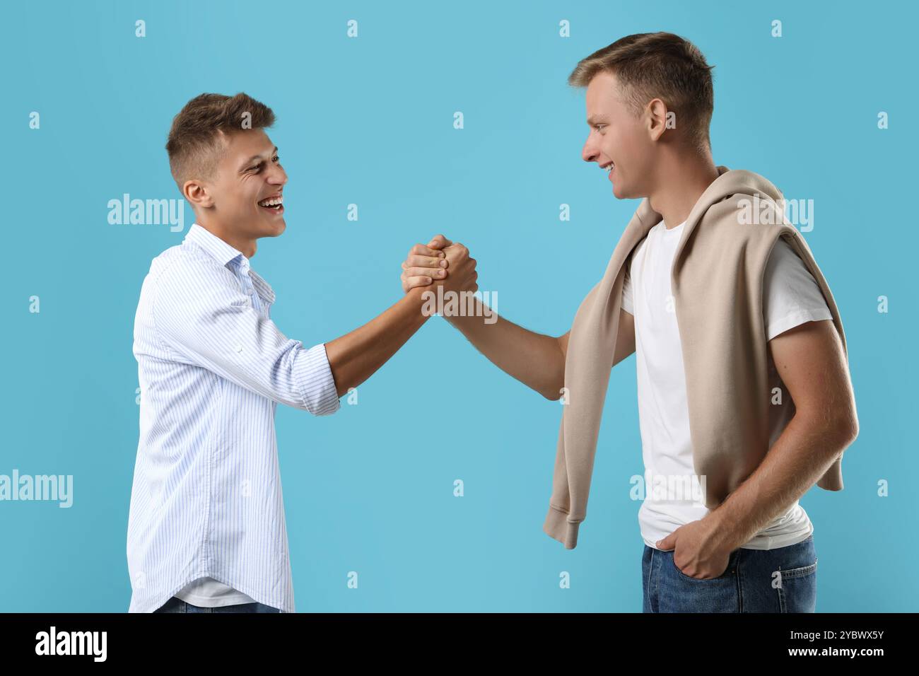 Happy brothers clasping hands on light blue background Stock Photo - Alamy