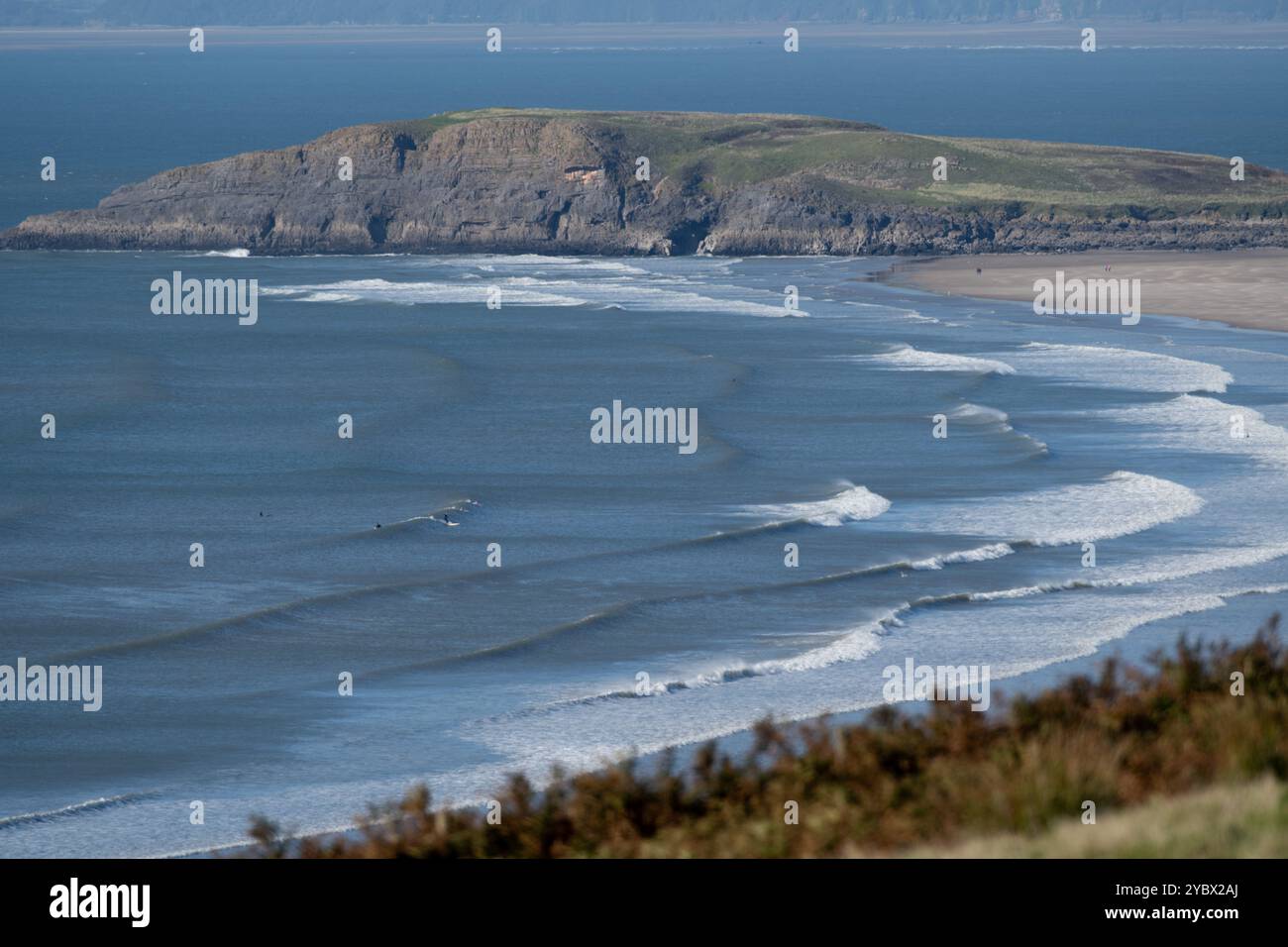 Surfing at Rhossili with lines of offshore surf . A surfer takes off on ...
